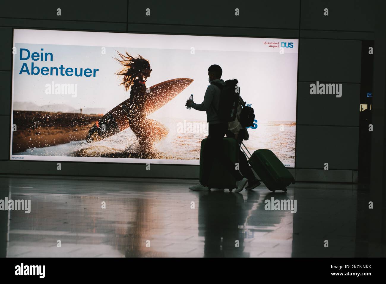 two travellers walk pass a big duesseldorf airport advertising sign at ...