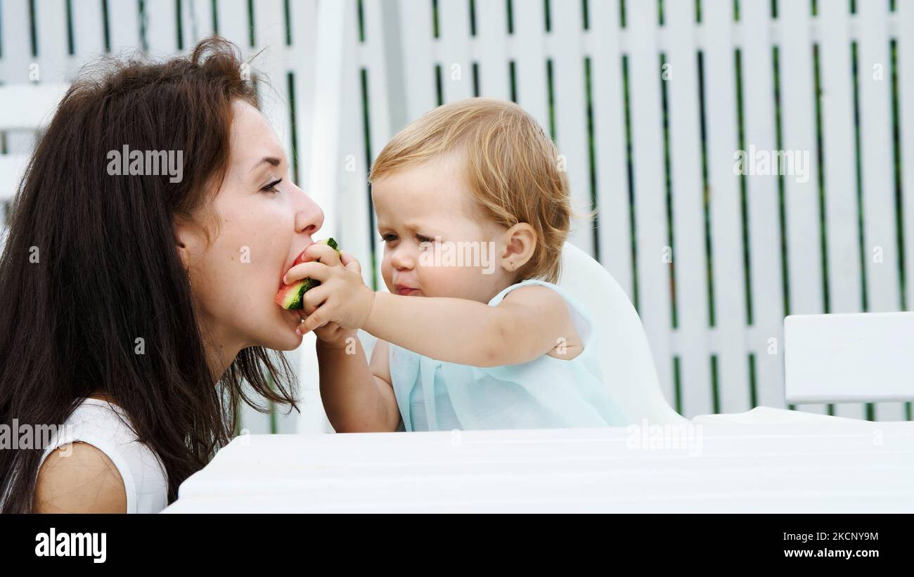 summer, in the garden, a funny one-year-old blonde girl treats her ...