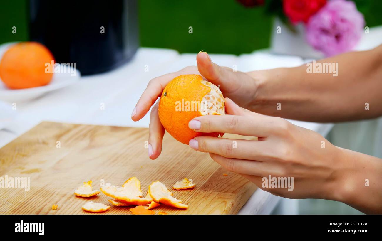 summer, in the garden, close-up, female hands are peeling an orange ...