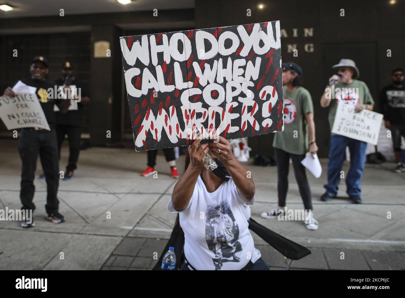 "Who do you call when cops murder?" A woman directs her sign toward the ...