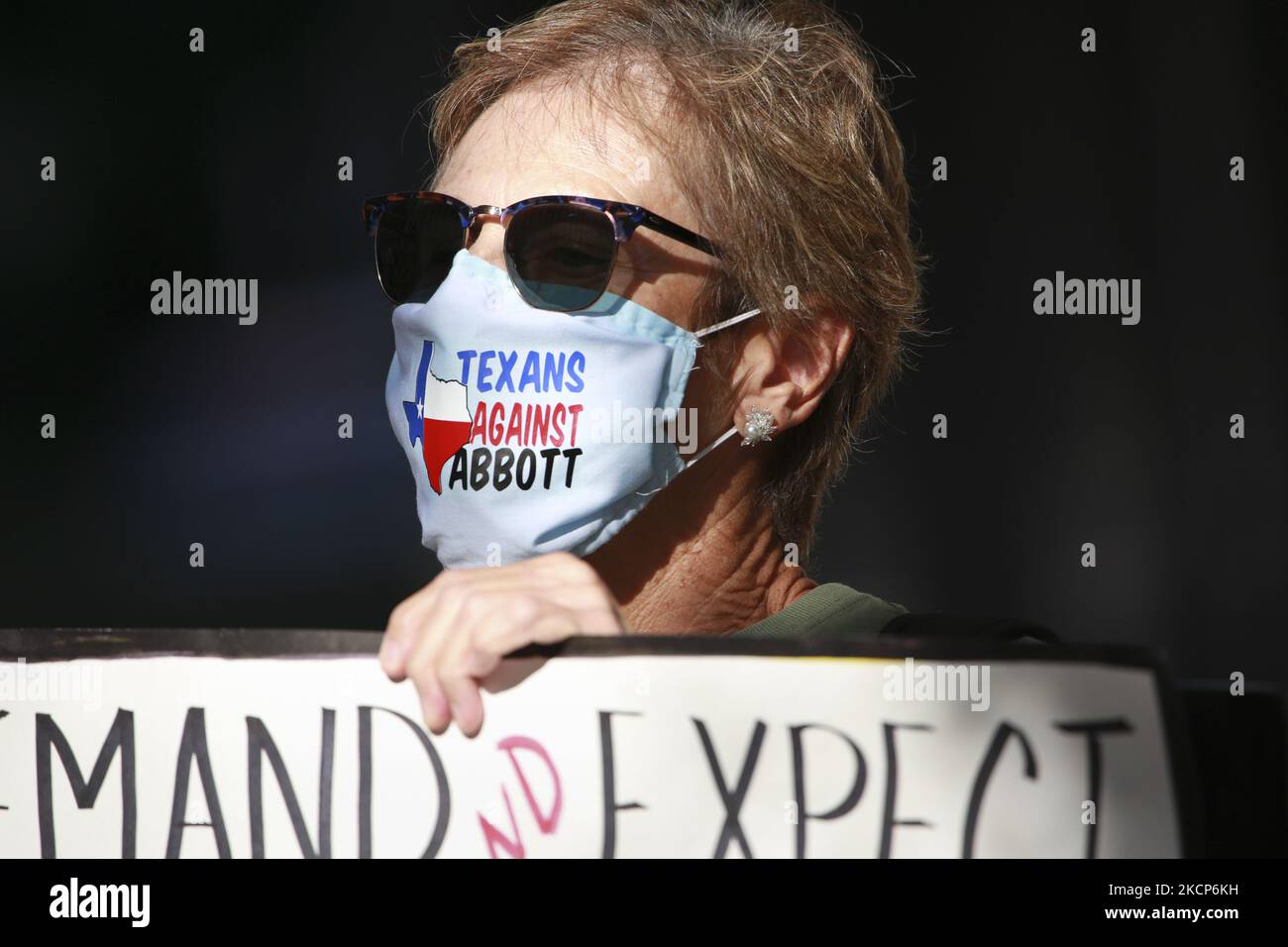 A protestor wears a mask that says, "Texans against Abbott," referring ...