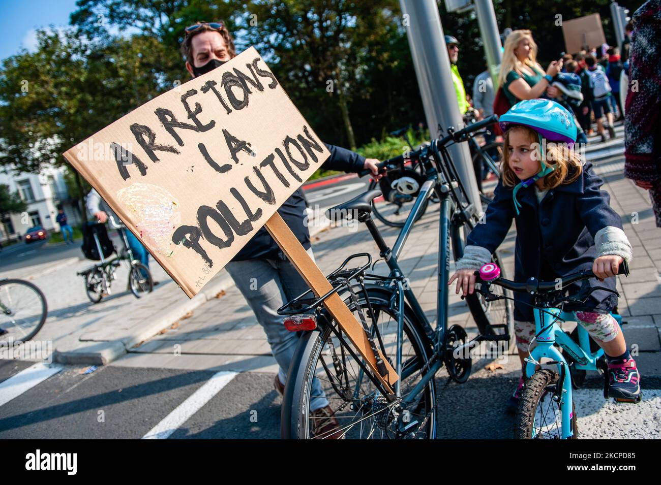 A little girl on a bike is looking at a placard that says Stop ...