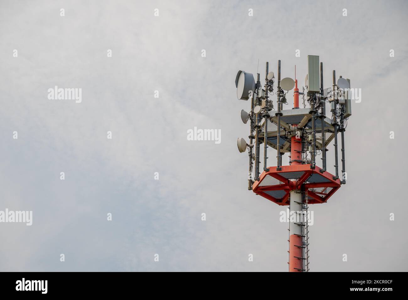 5G telecommunications tower and microwave antennas on a red white mast set against cloudy sky ...
