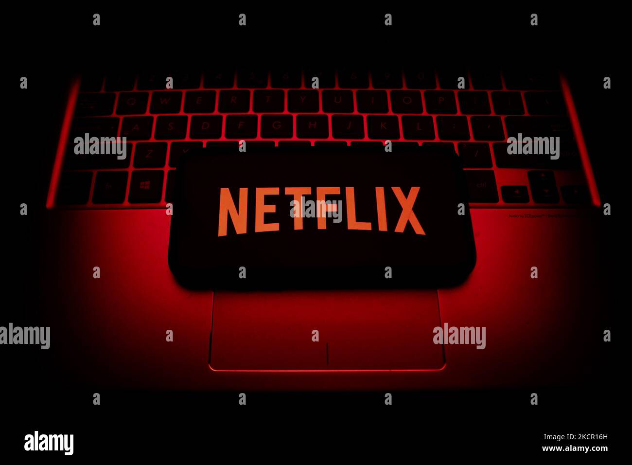 Netflix logo displayed on a phone screen and a laptop keyboard are seen ...