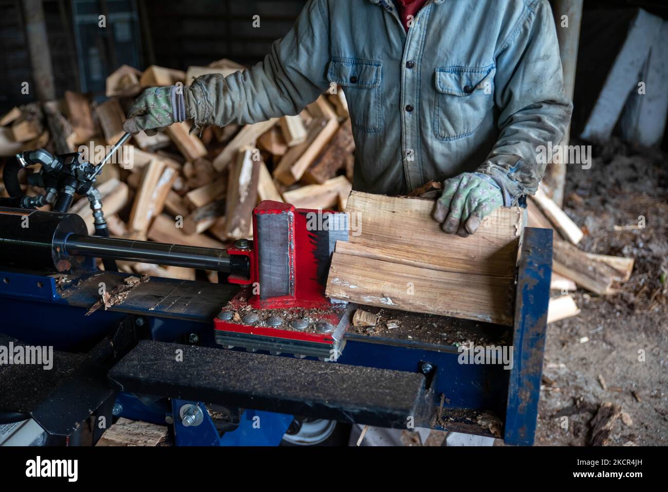 Hydraulic log splitter blade cuts into wood with workman and woodpile ...