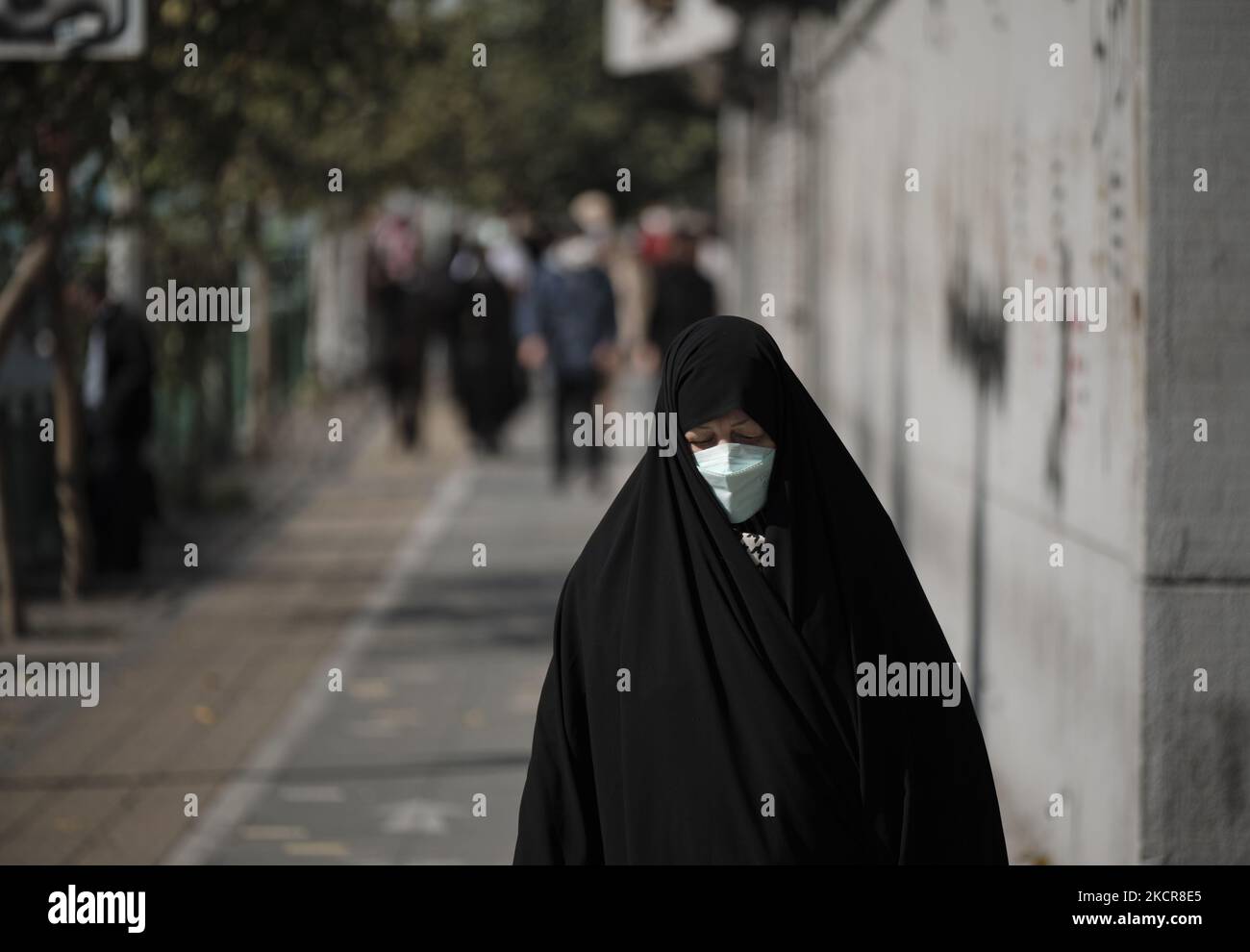 An Iranian veiled woman wearing a protective face mask walks along an ...