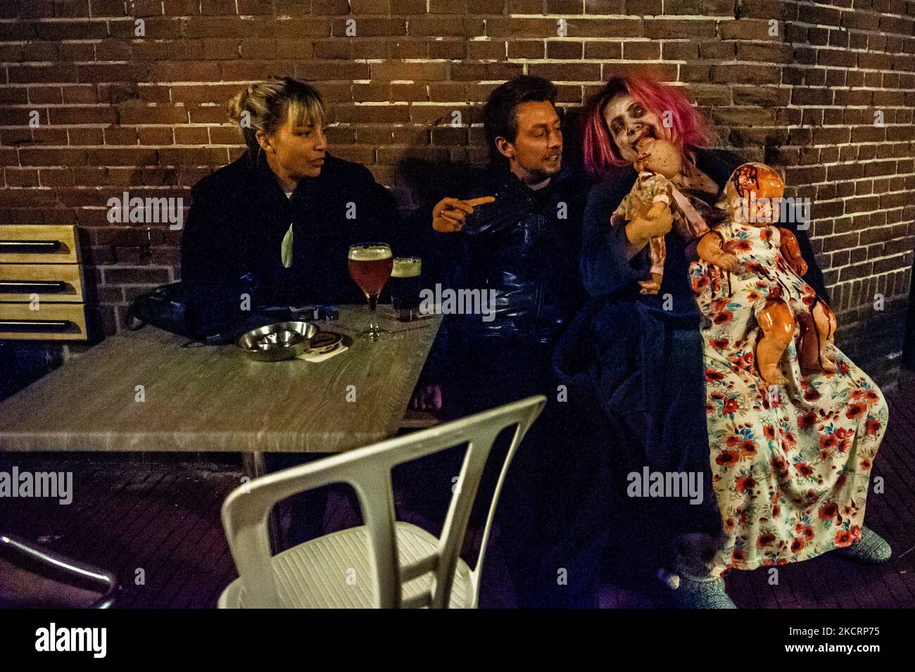 A female zombie carrying fake babies is sitting with a couple on a ...