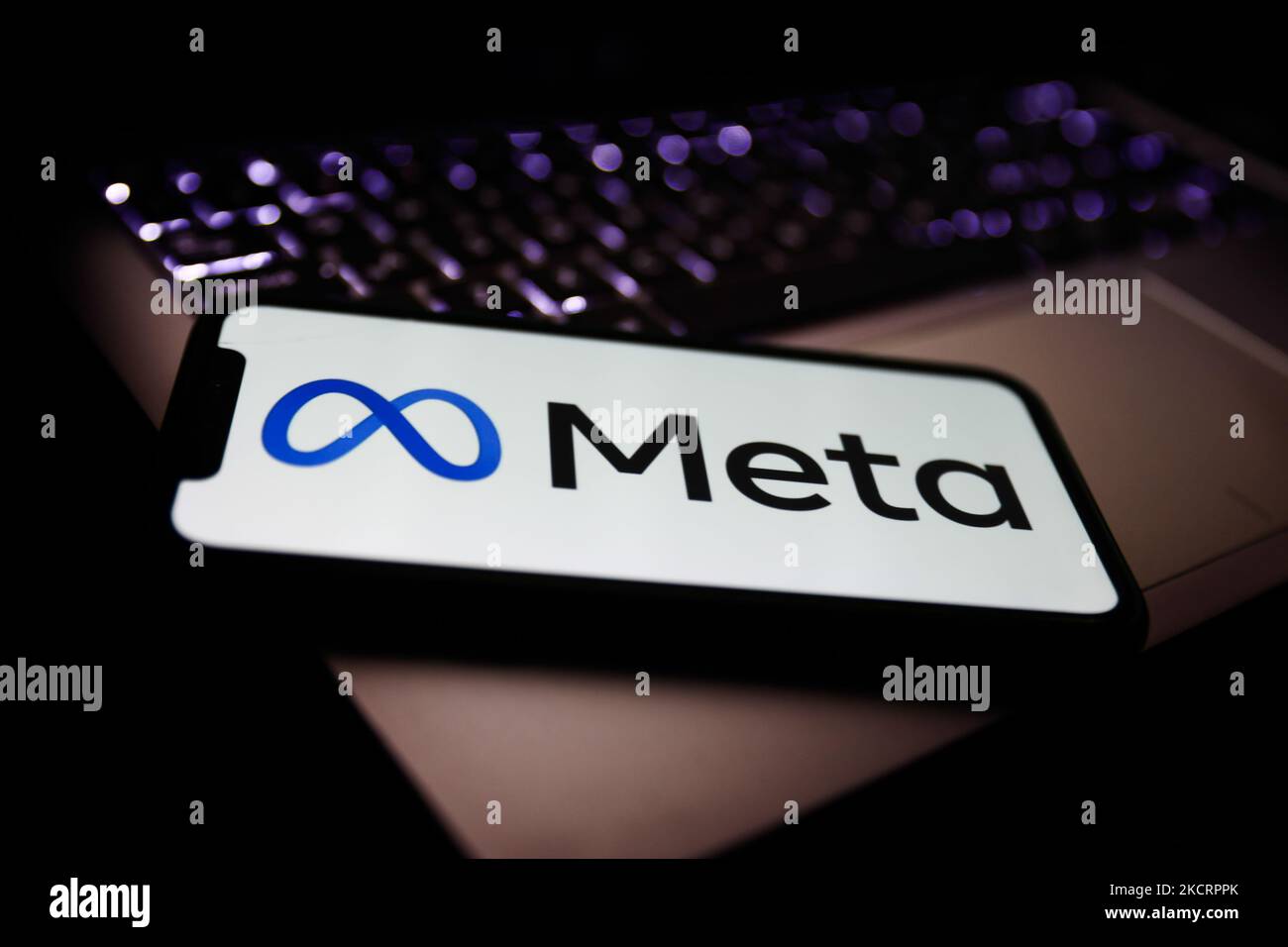 Meta logo displayed on a phone screen and a laptop keyboard are seen in ...