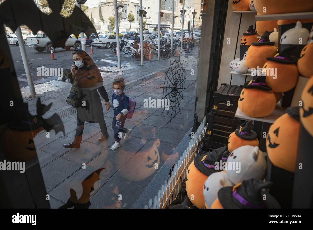 An Iranian woman and her young daughter walk past a shop window that is ...