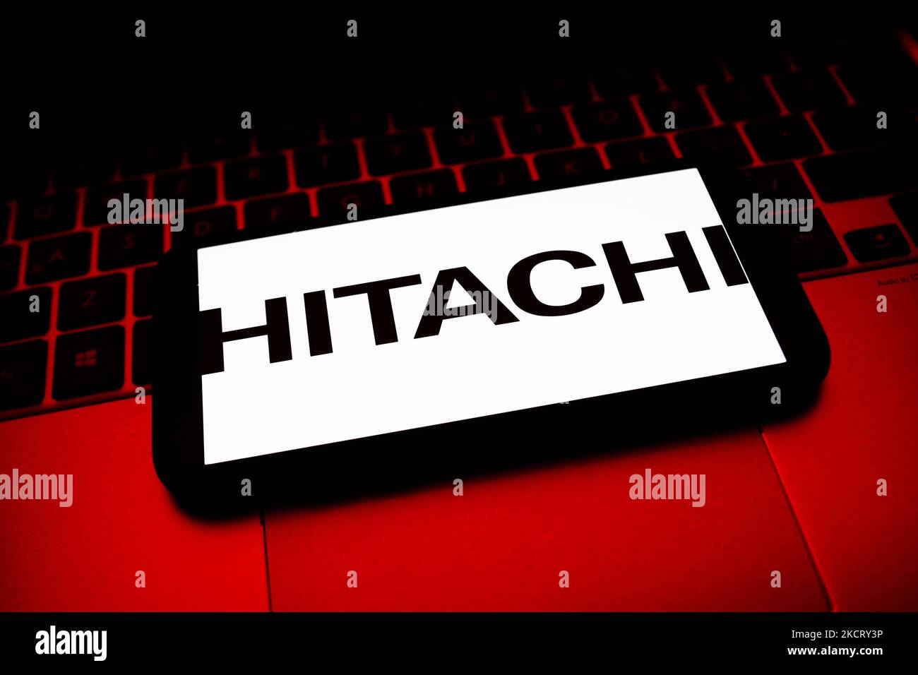 Hitachi logo displayed on a phone screen and a laptop keyboard are seen ...