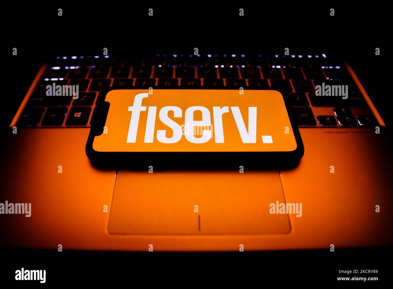 Fiserv logo displayed on a phone screen and a laptop keyboard are seen ...