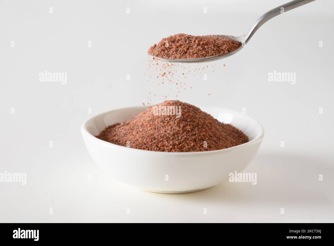 Pouring Indian Black salt Kala namak in bowl on white background. Close ...