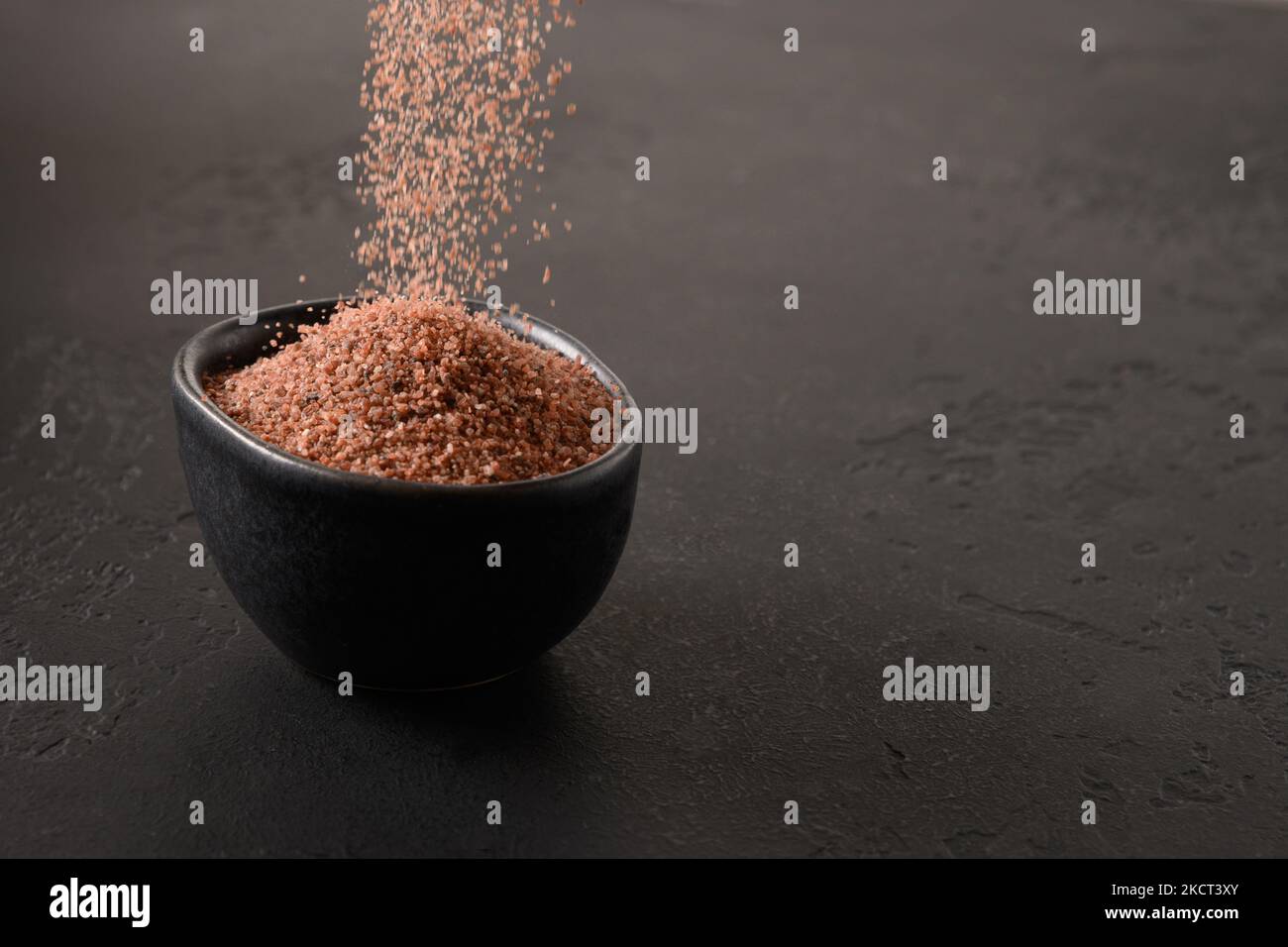 Pouring Indian Black salt Kala namak in bowl on black background. Close ...