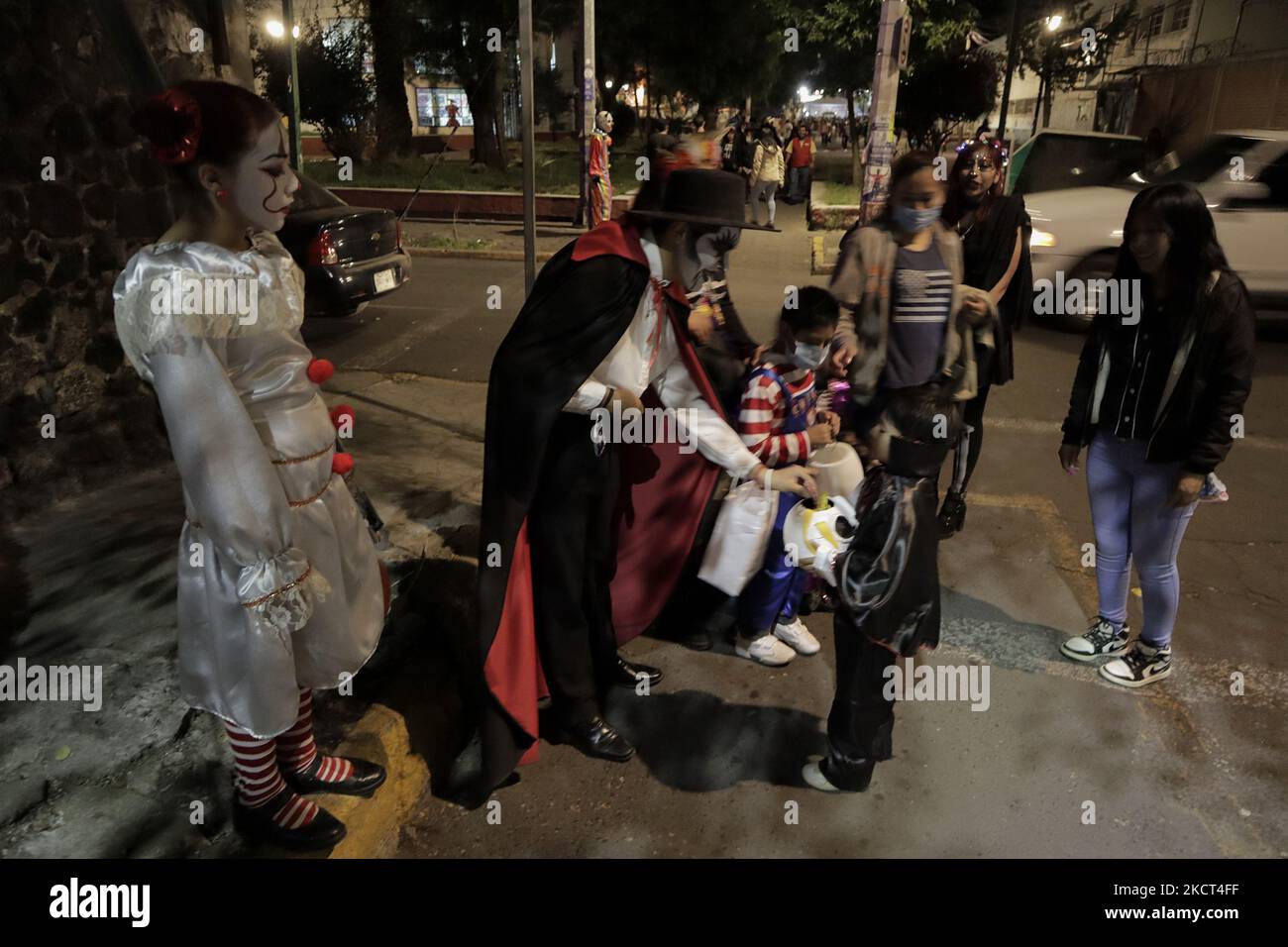 An adult dressed as a vampire hands out sweets to children near the San ...