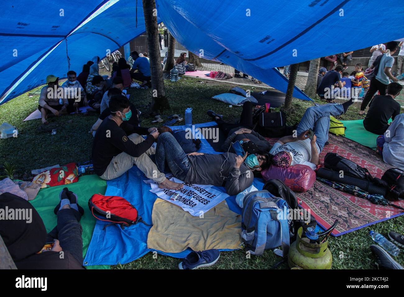 Afghan refugee men living in Indonesia rest by their phone in tent ...