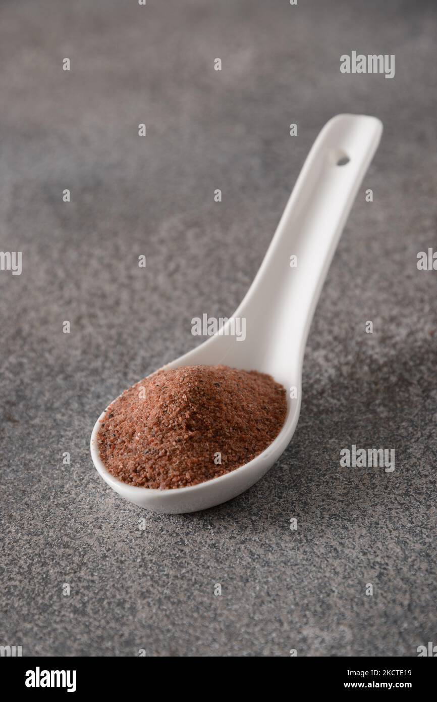 Pouring Indian Black salt Kala namak in served bowl on gray background ...