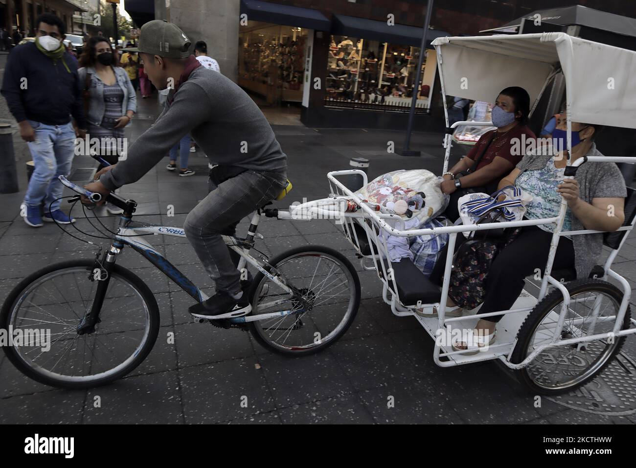 A bicycle taxi driver transports a group of people in the streets of ...