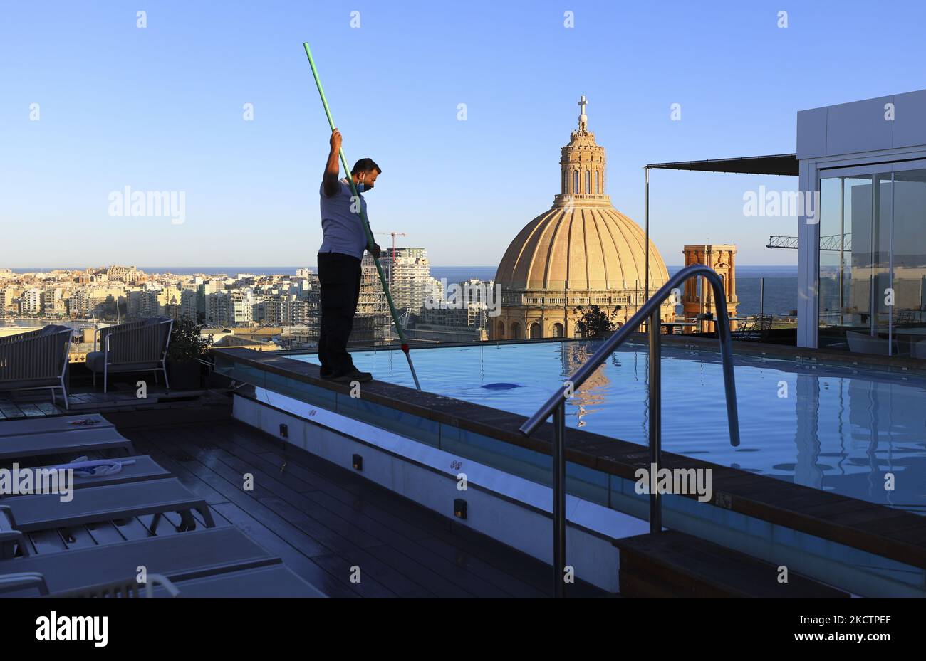 A hotel worker cleans a rooftop pool in front of St. Paul's Cathedral ...