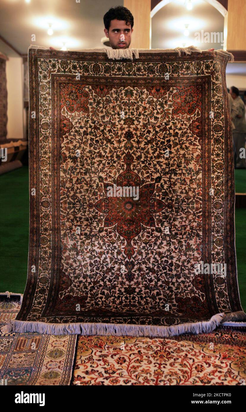 Kashmiri salesman shows a hand-knotted silk Kashmiri carpet in a ...
