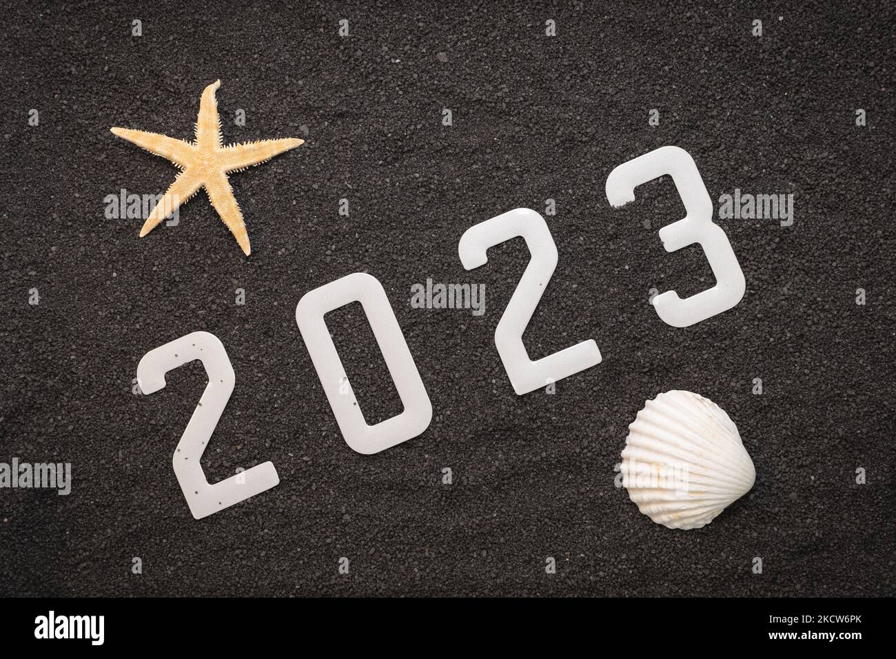 Happy New Year 2023 concept with a shell and a starfish on black beach ...