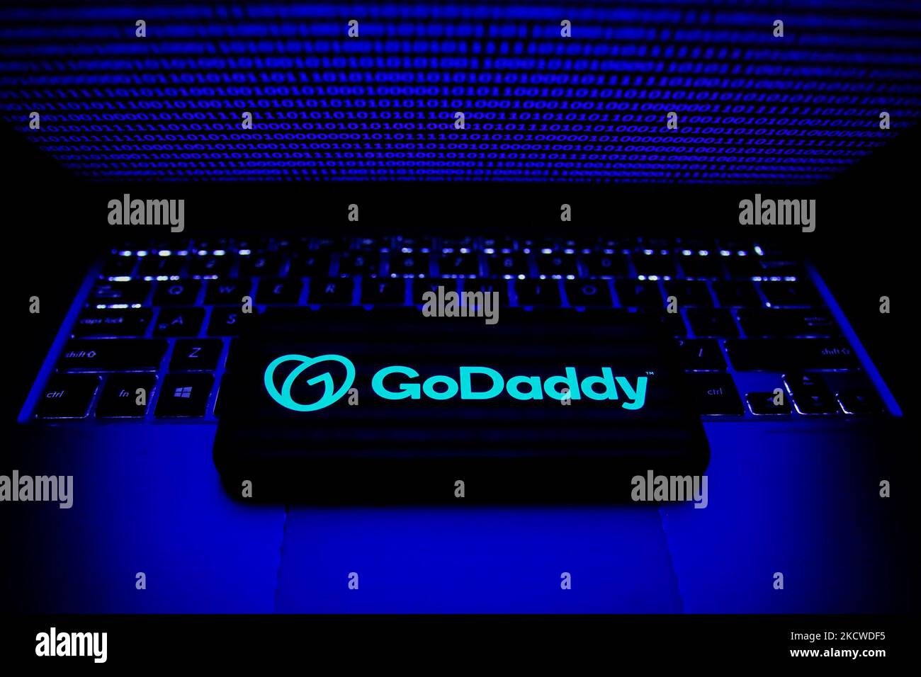 GoDaddy logo displayed on a phone screen and binary code displayed on a ...