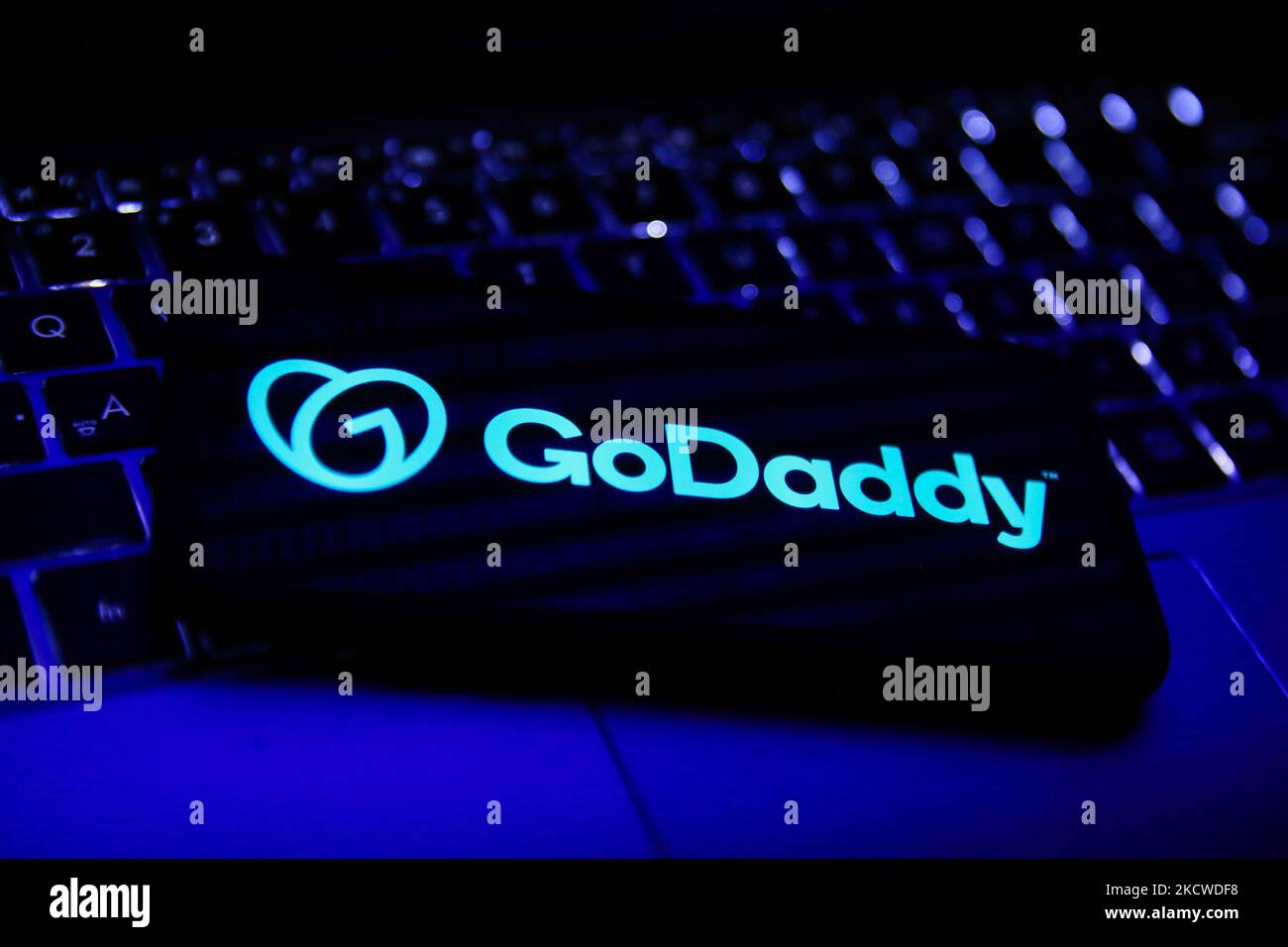 GoDaddy logo displayed on a phone screen and a laptop keyboard are seen ...