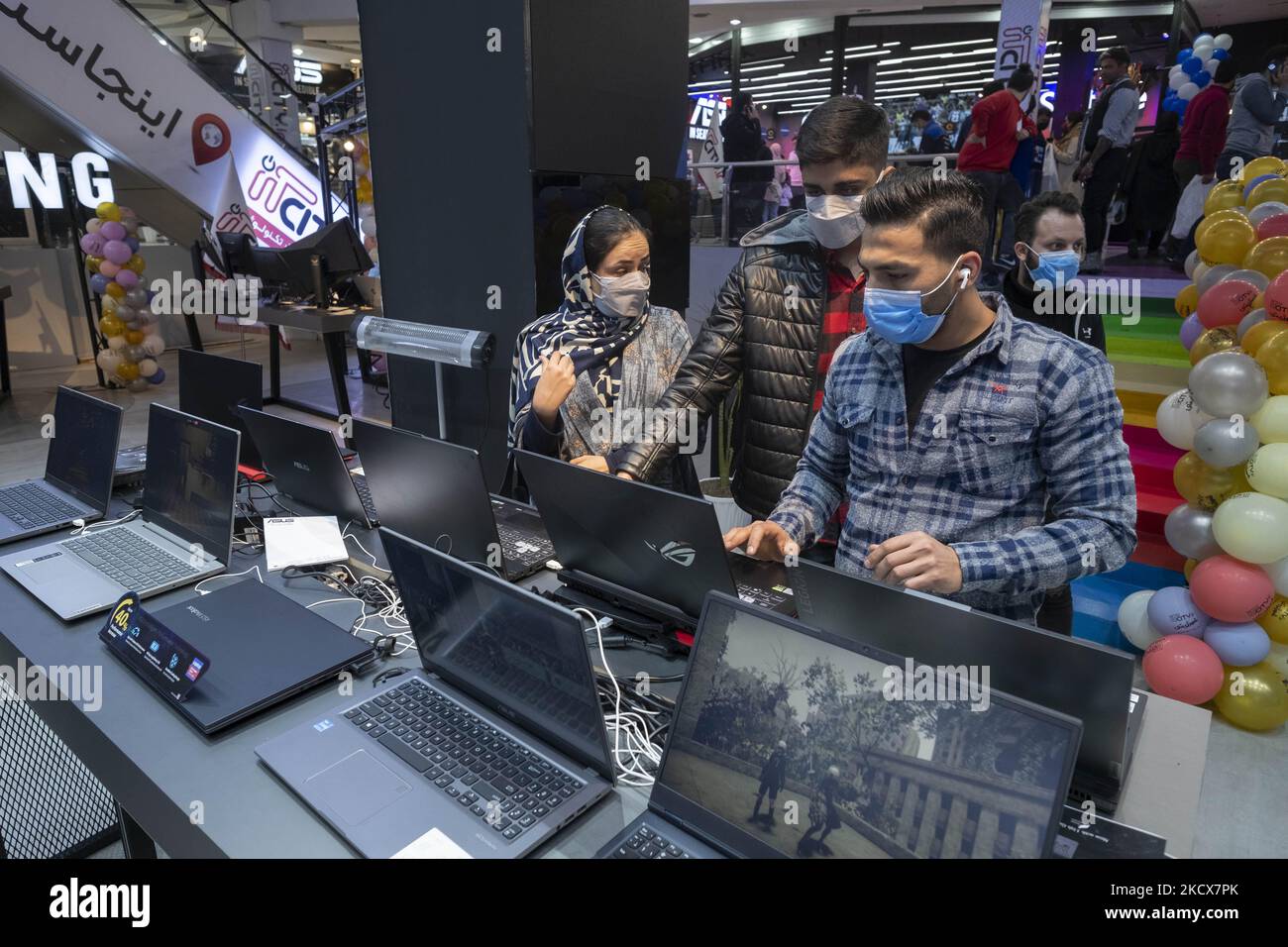 An Iranian family wearing protective face masks look at laptops while ...