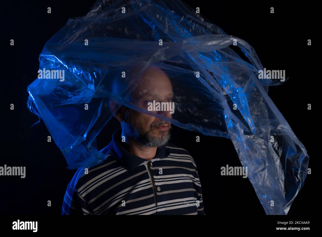 Mature man with a transparent plastic blue bag flying over his head and ...