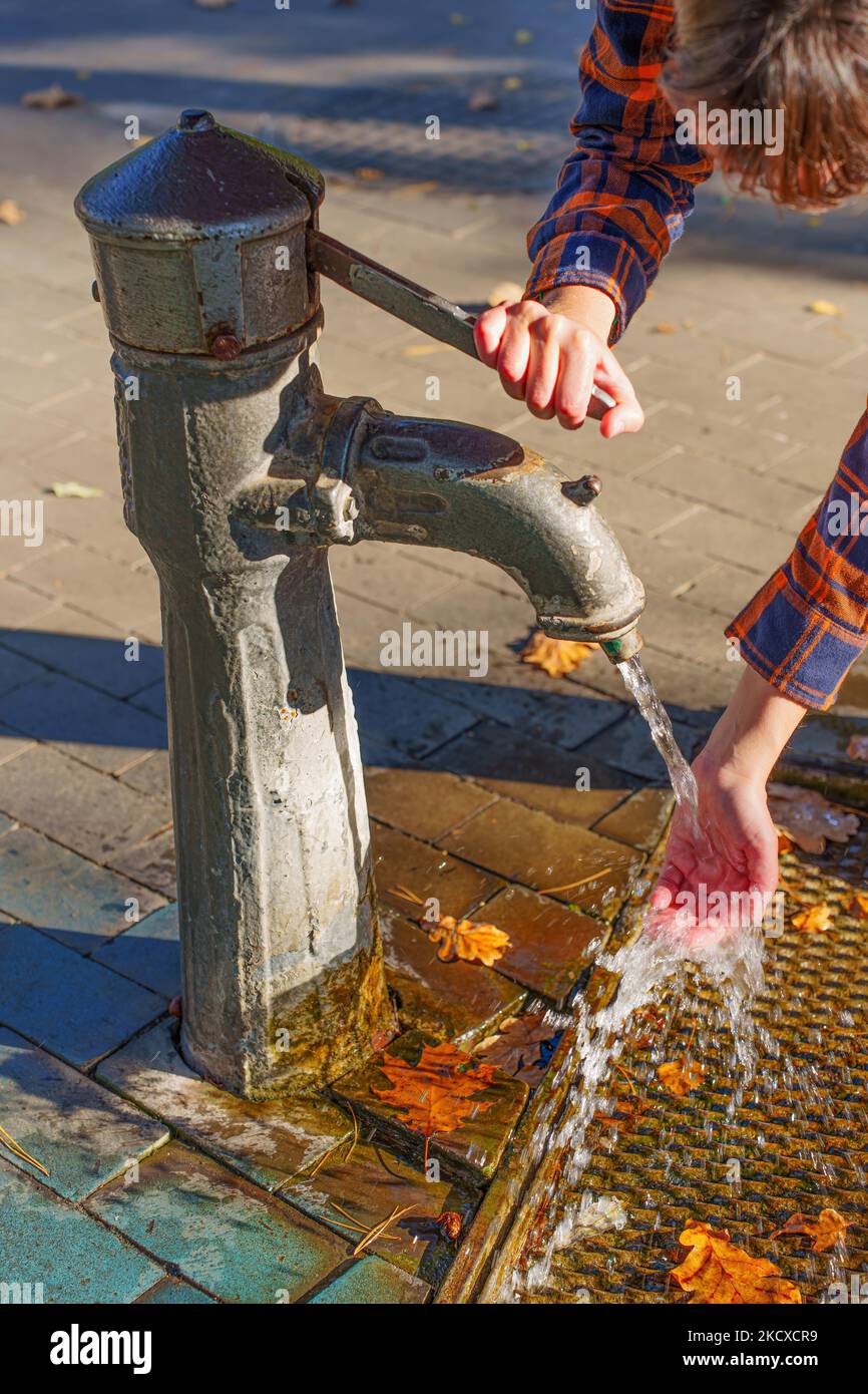 Female uses a hand pump to wash hands at a public drinking water well ...