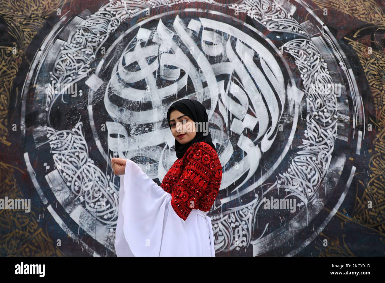 A Palestinian girl wearing traditional dress creation past a art mural ...