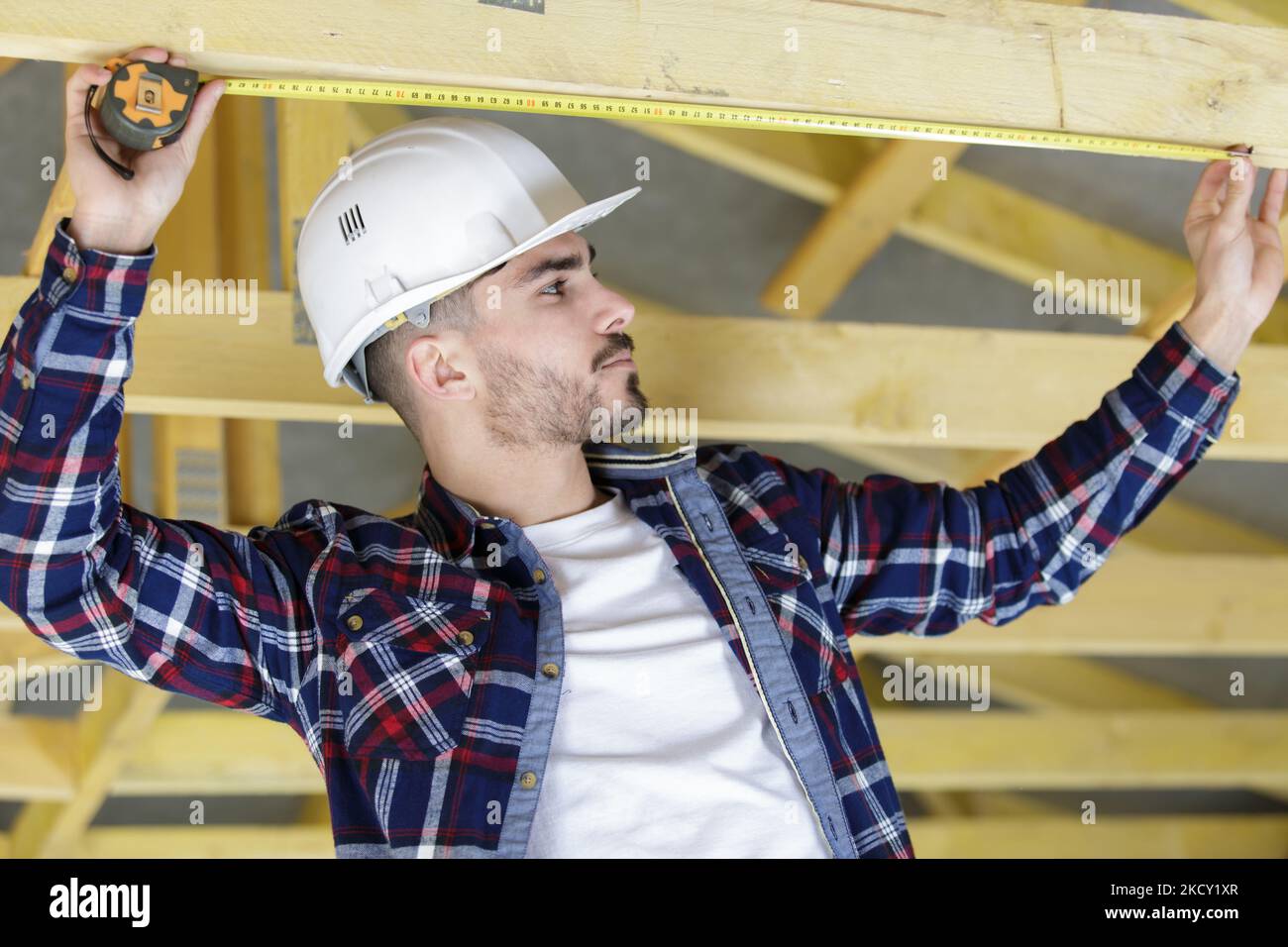worker measuring between boards with tape measure at construction site ...