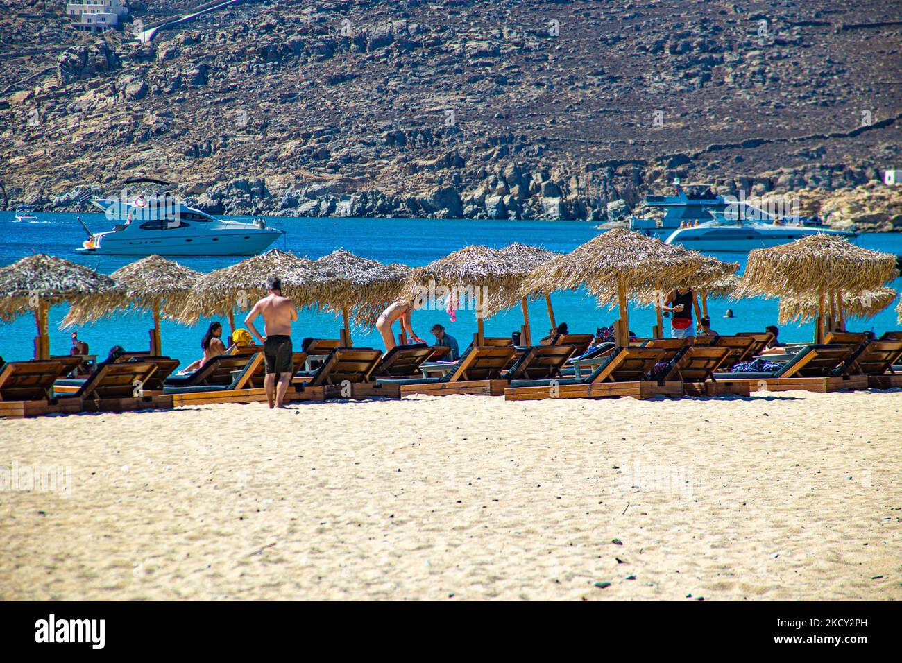 The beach bar with the umbrellas and sunbeds at the shore. Tourists as ...