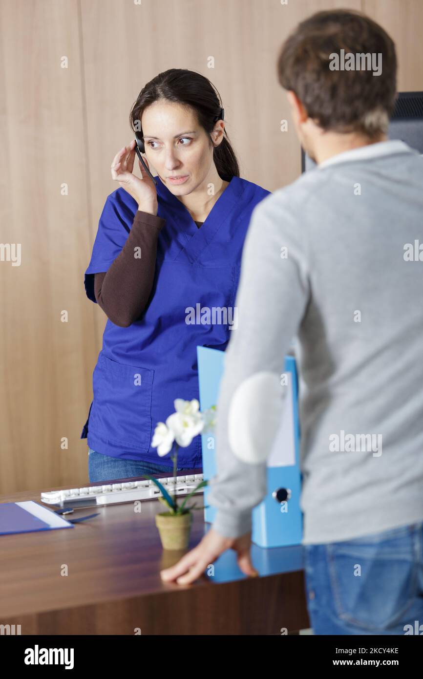medical secretary taking call while patient waits at counter Stock ...