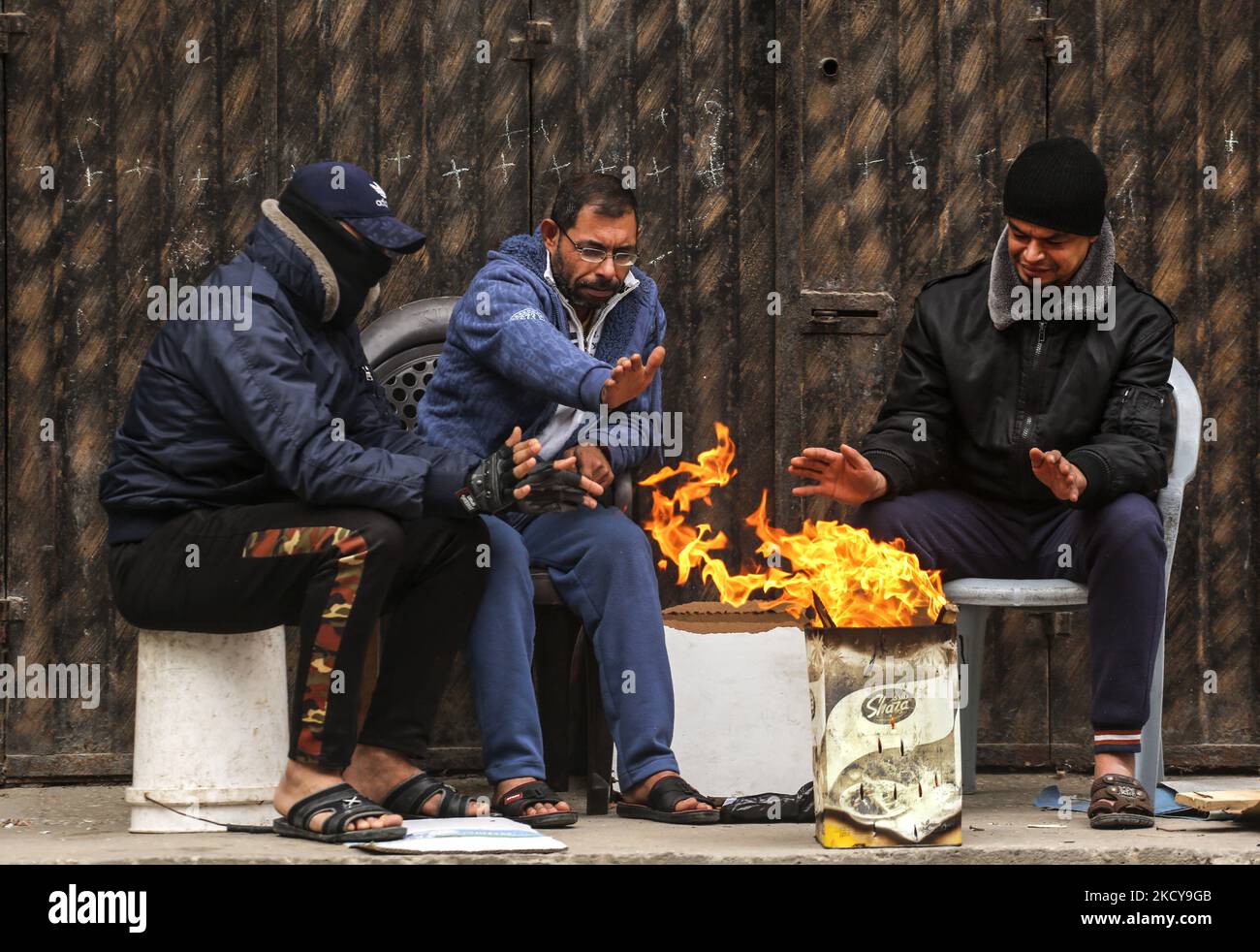 Palestinian refugees sit around the fire outside their home to warm ...