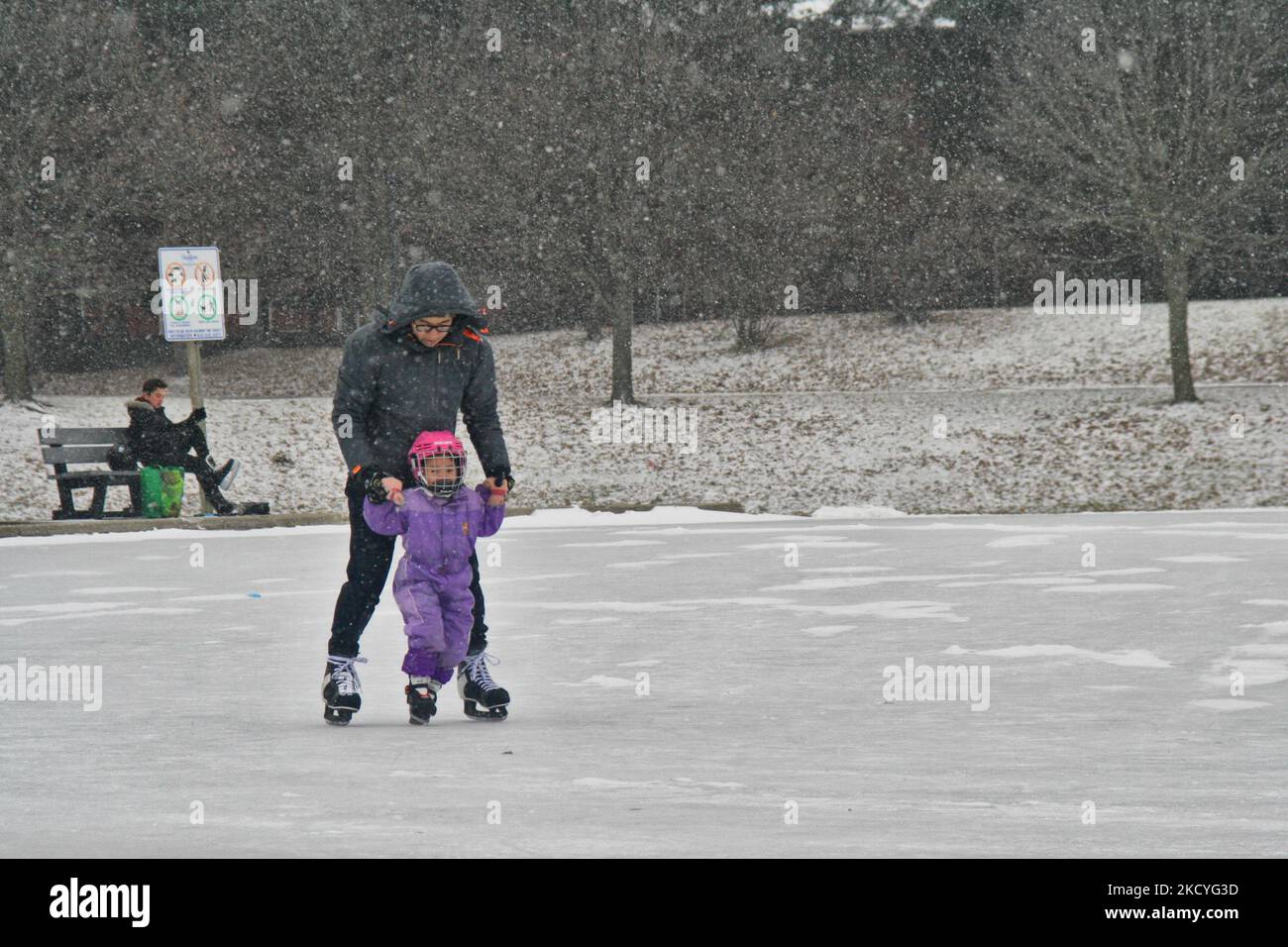 People ice skating on an outdoor ice rink as a mix of light snow and ...