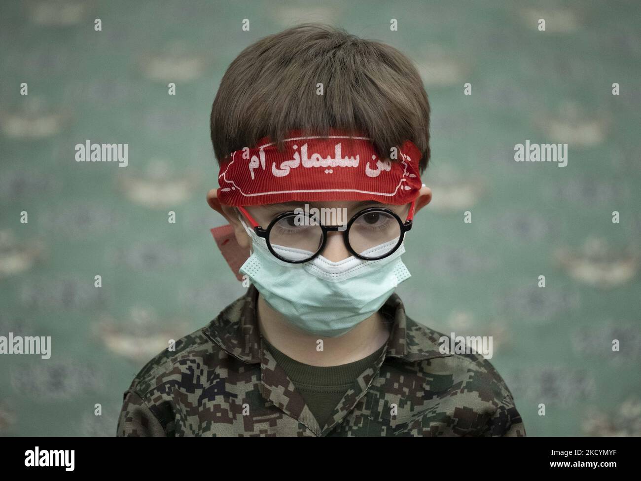 An Iranian young boy in military uniforms wearing a red headband with a ...