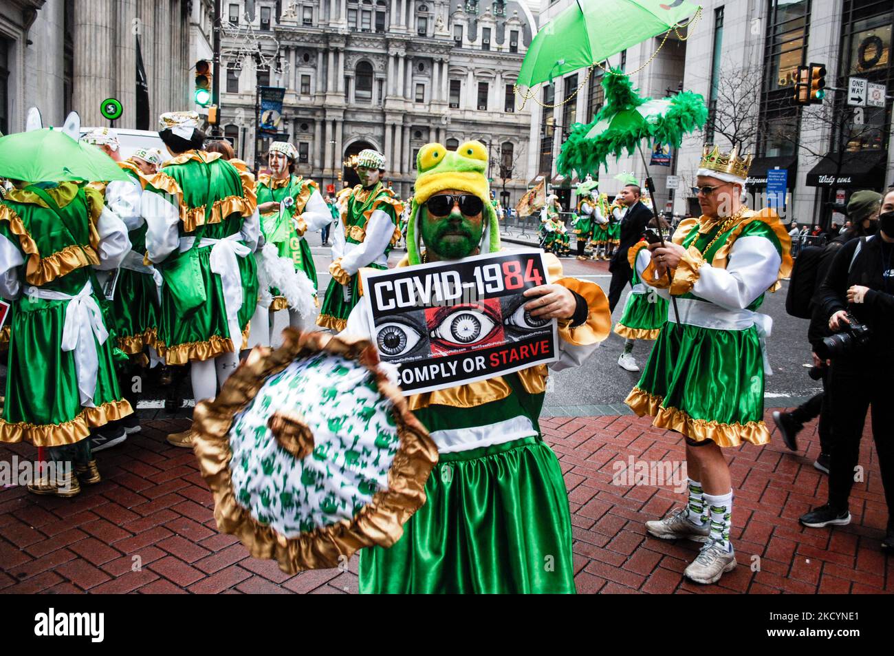 A froggy Carr Mummer holds a sign comparing Philadelphia’s vaccine ...
