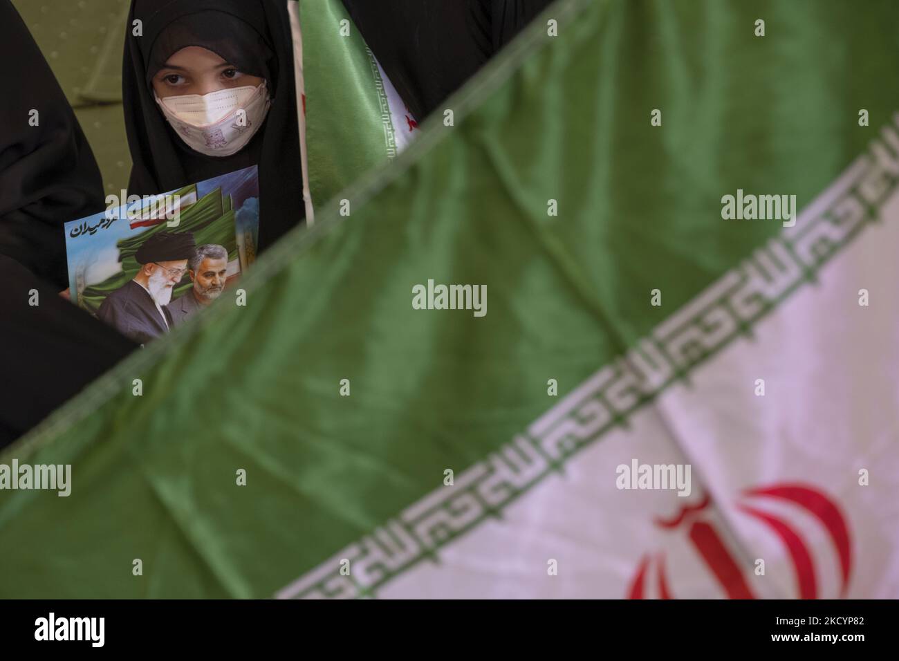 An Iranian young girl wearing a protective face mask holds a poster ...