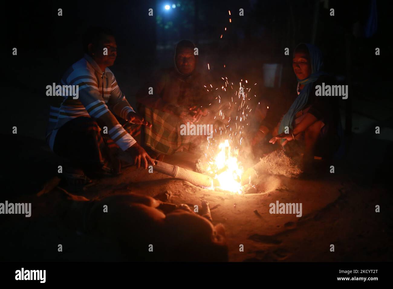 People warm themselves around a bonfire on a cold evening in Mymensingh ...