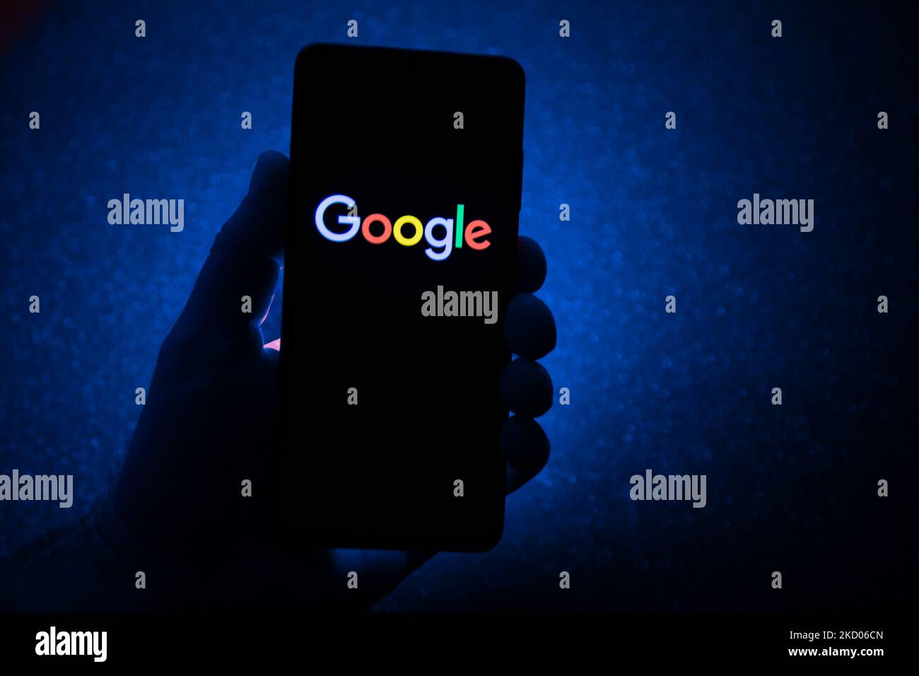 Hand is holding a smartphone with the Google logo displayed and dark blue background. Google ...