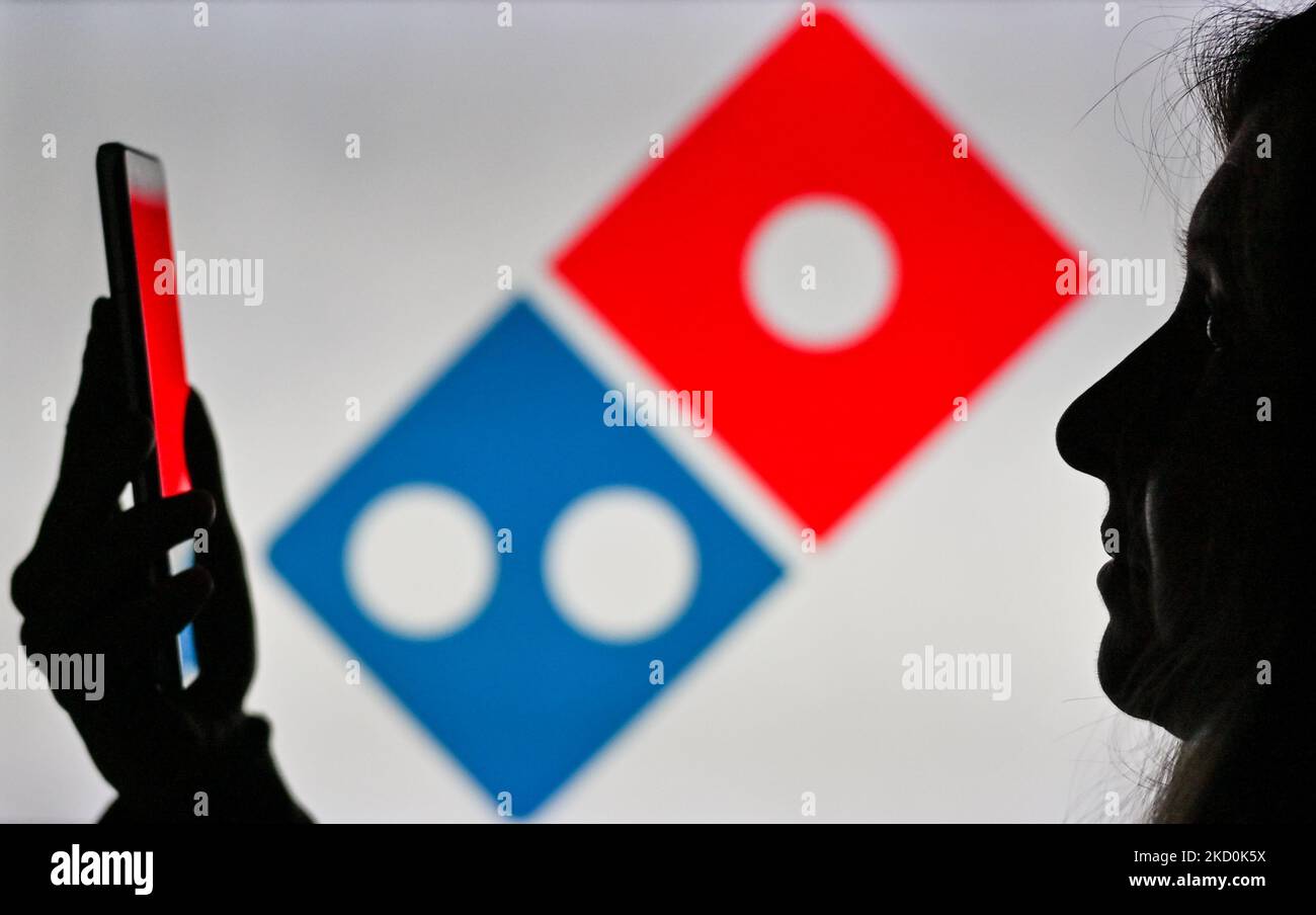 An image of a woman holding a cell phone in front of a Domino's Pizza ...