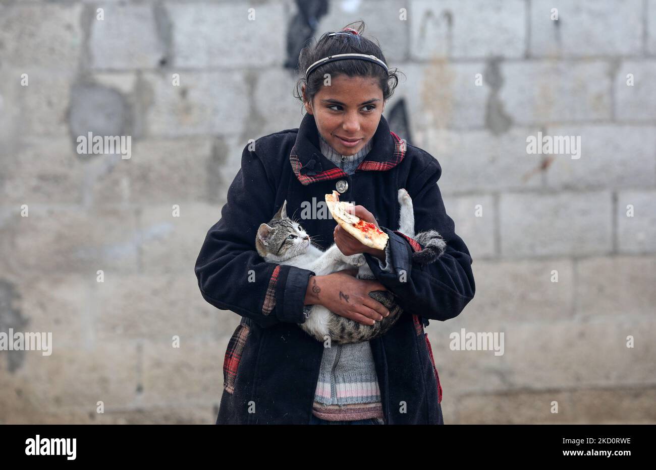 A Palestinian girl holds a cat in a poor neighborhood on a rainy day in ...
