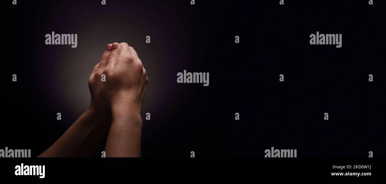 Praying hands with faith in religion and belief in God over dark ...
