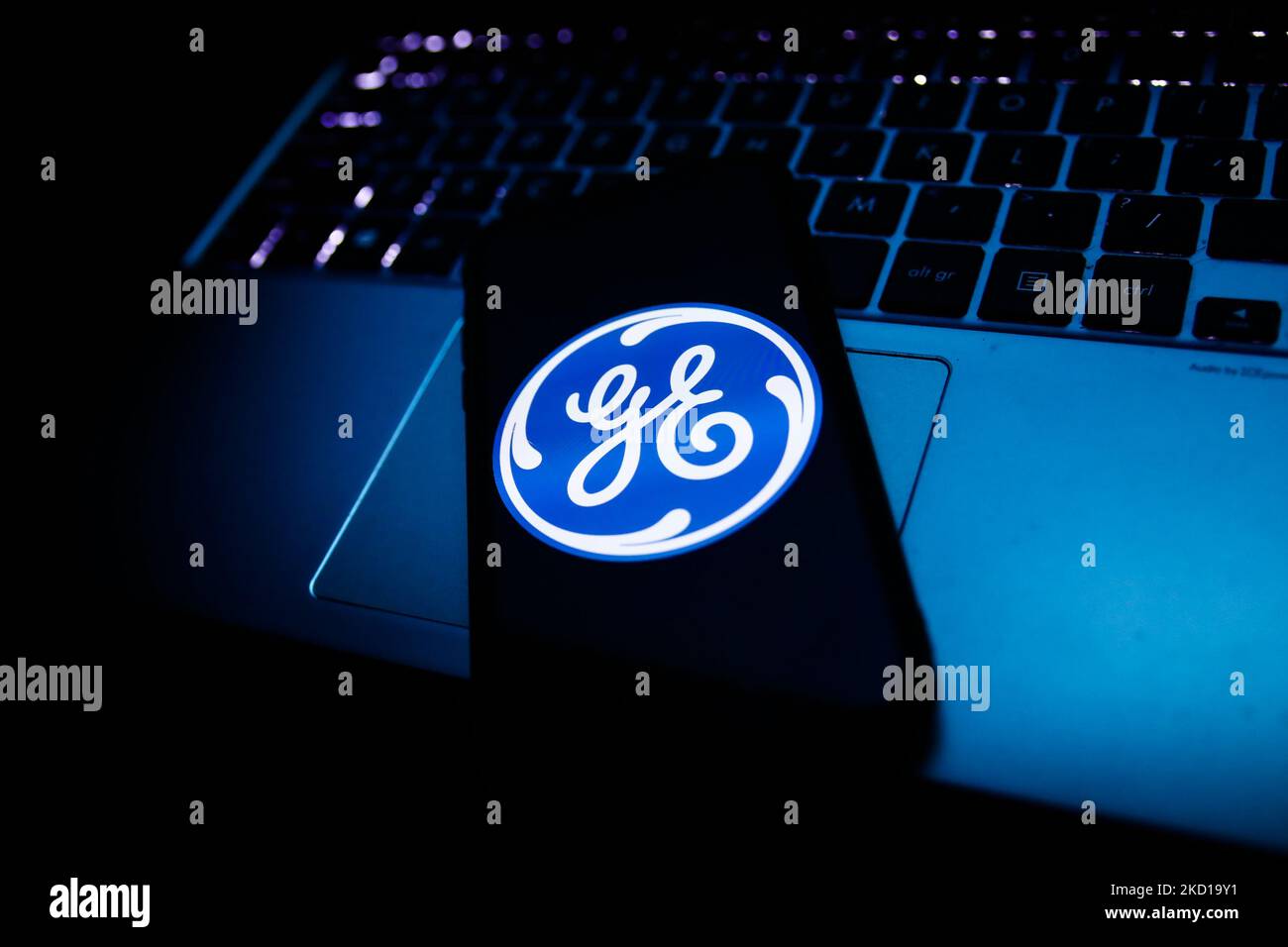 GE logo displayed on a phone screen and a laptop keyboard are seen in ...