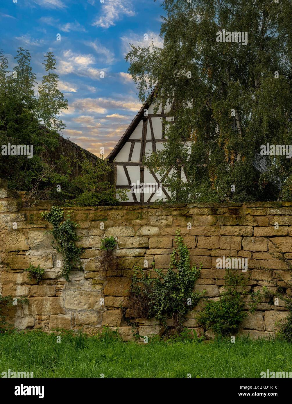 old half-timbered house behind an old quarry stone wall with trees and ...