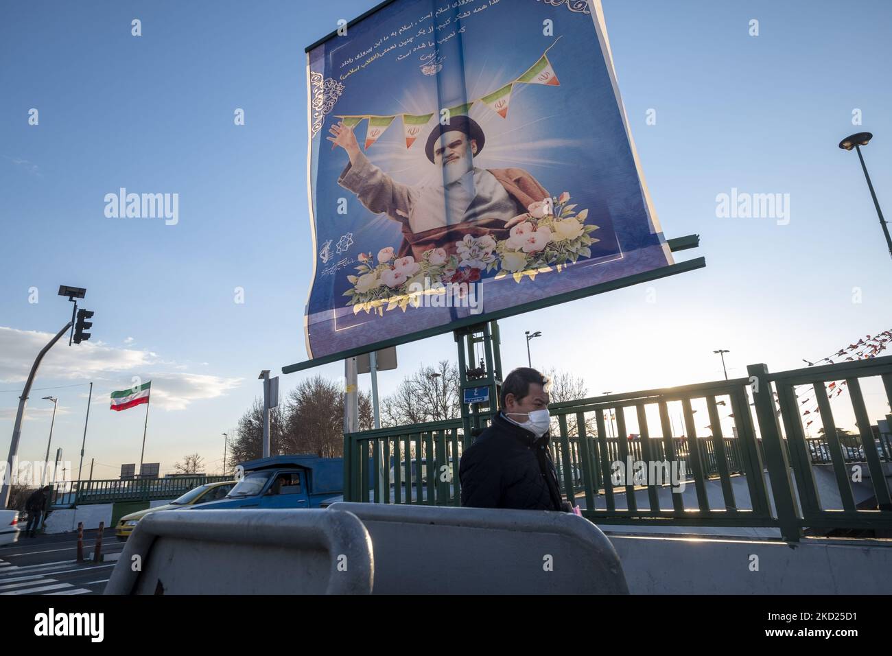 An Iranian man wearing a protective face mask walks under a portrait of ...