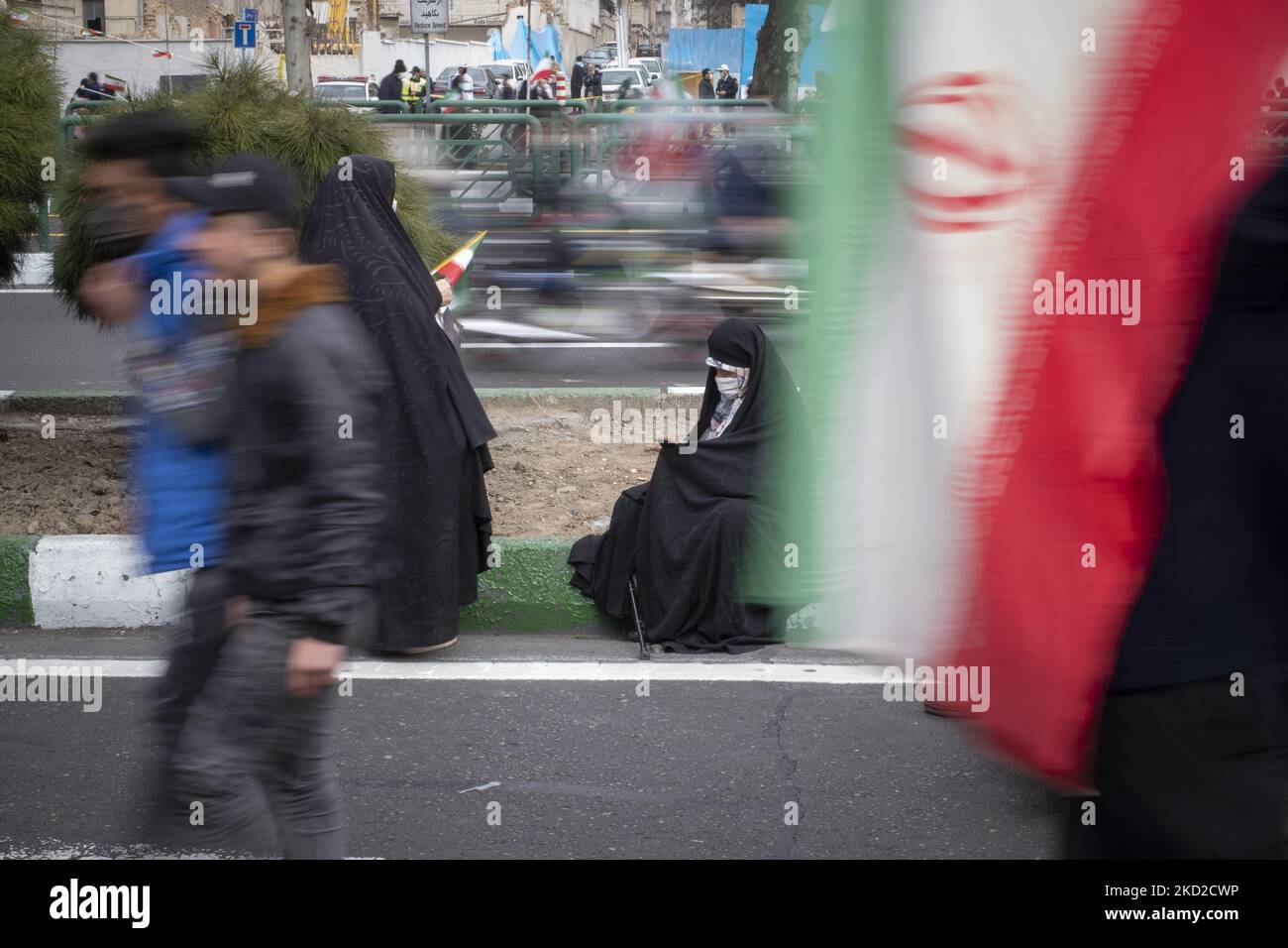 An Iranian veiled woman wearing a protective face mask sits on a corner ...