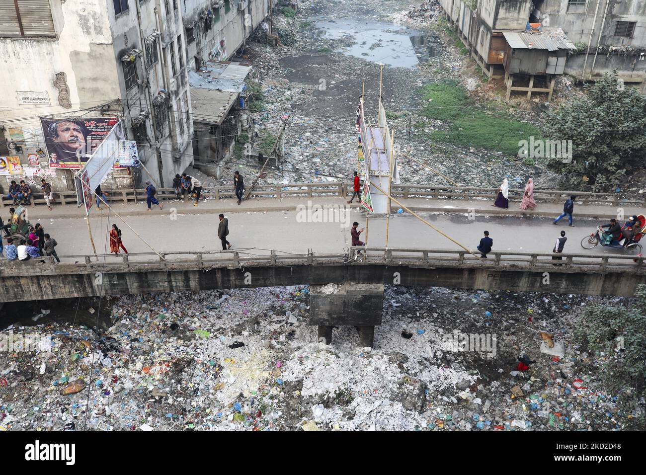People walk along a bridge over a polluted area in Dhaka, Bangladesh on ...