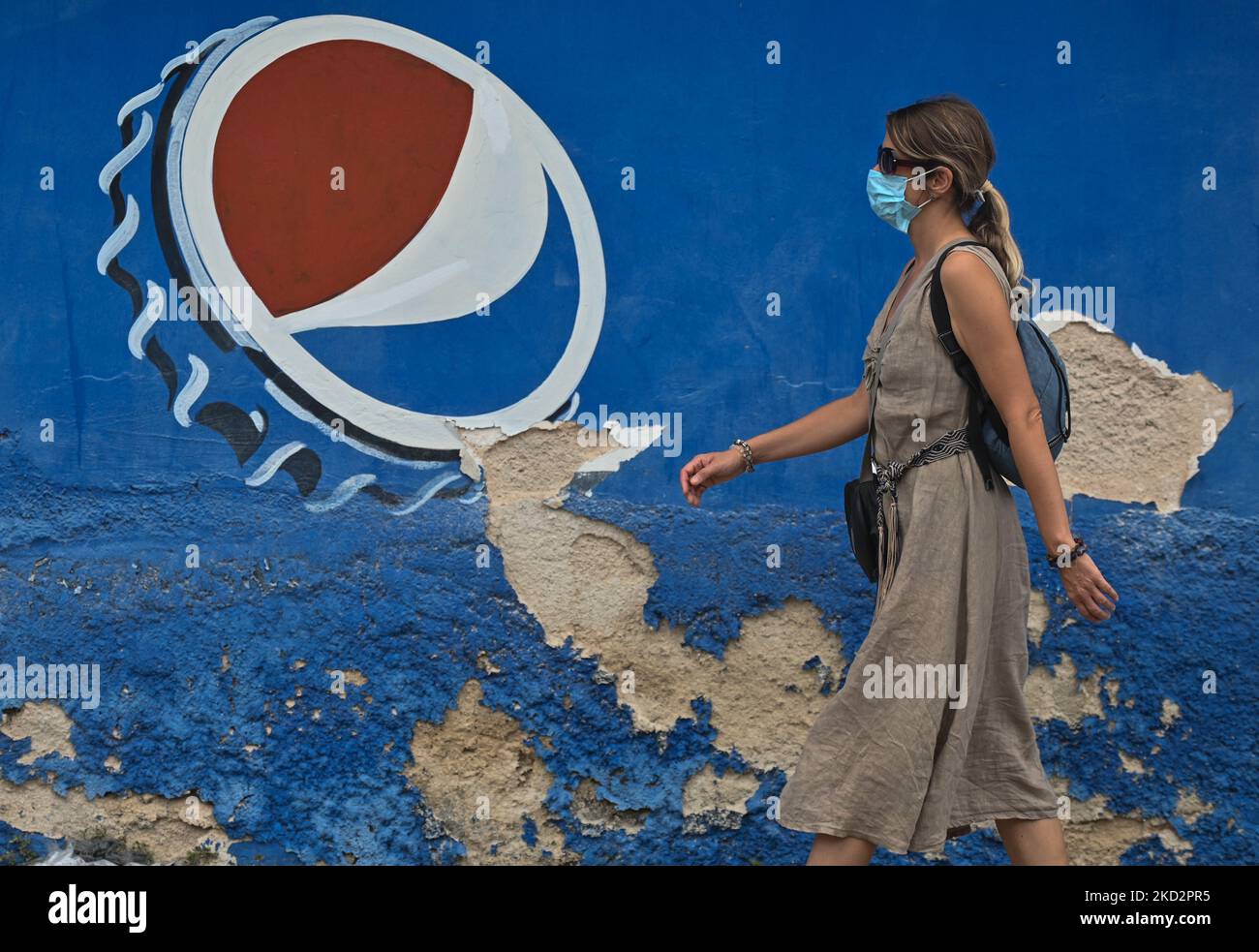 A woman wearing a face mask walks past a Pepsi ad in Merida center. On ...