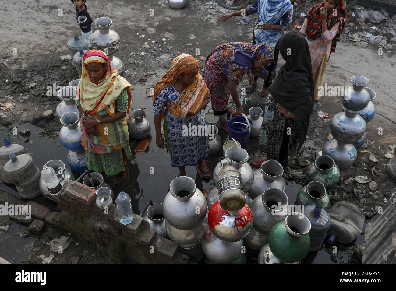 Women are filling jugs with drinking water in a water supply at a slum ...